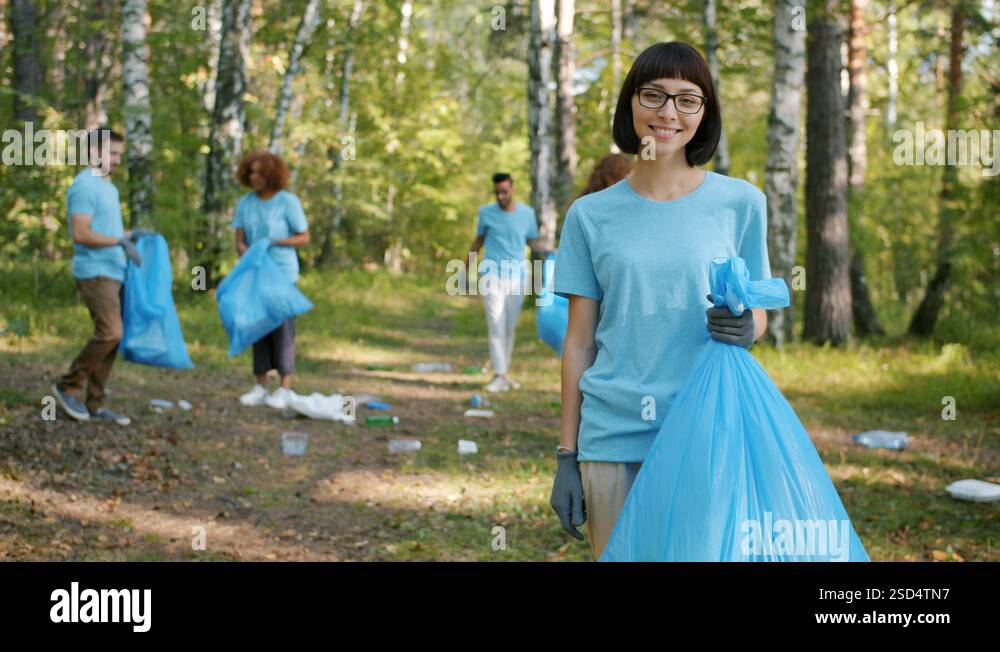 Pretty female volunteer looking at camera holding trash bag in polluted ...