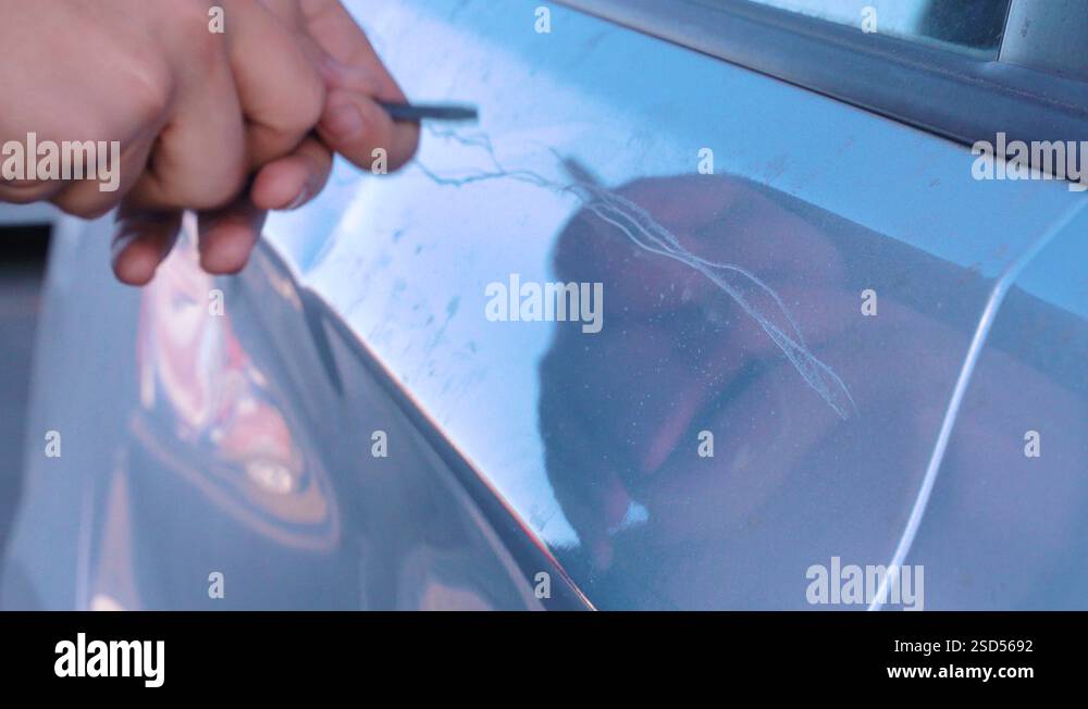 Bad guy scratching the car door with a screwdriver in the parking lot ...