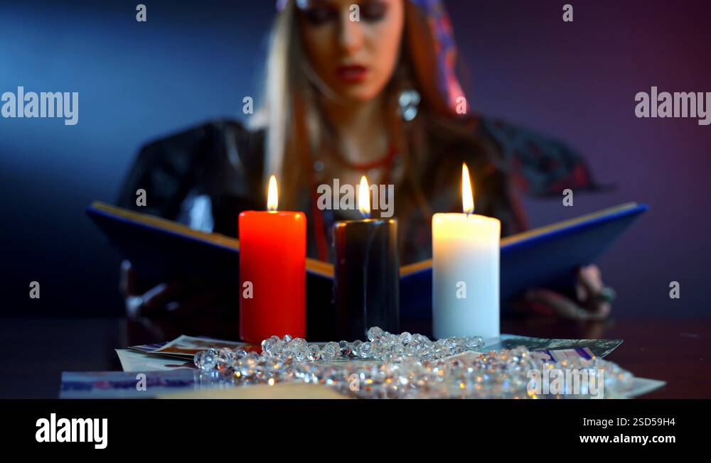 Scary young witch holding devil book and reading spell in dark room ...