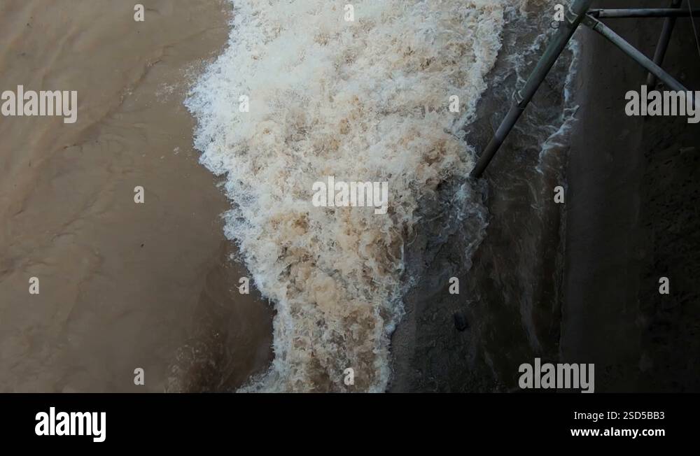 Slow motion tilt up close up brown dirty water flowing in concrete ...