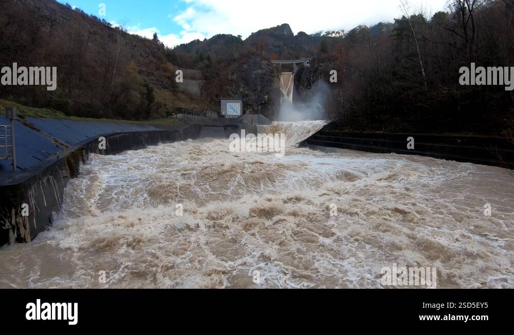 Right pan dirty turbulent flood water leaving dam in narrow Alps valley ...