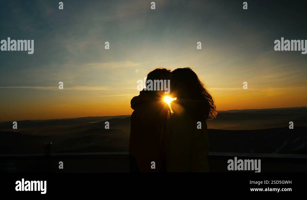 couple in love kisses standing on snowy slope at back sunset Stock ...