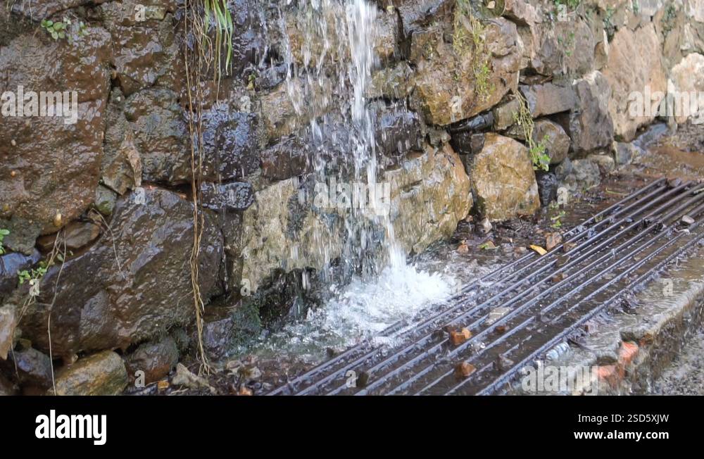 Rainfall wada falls in a stream on a sewer grate near a wall of raw ...