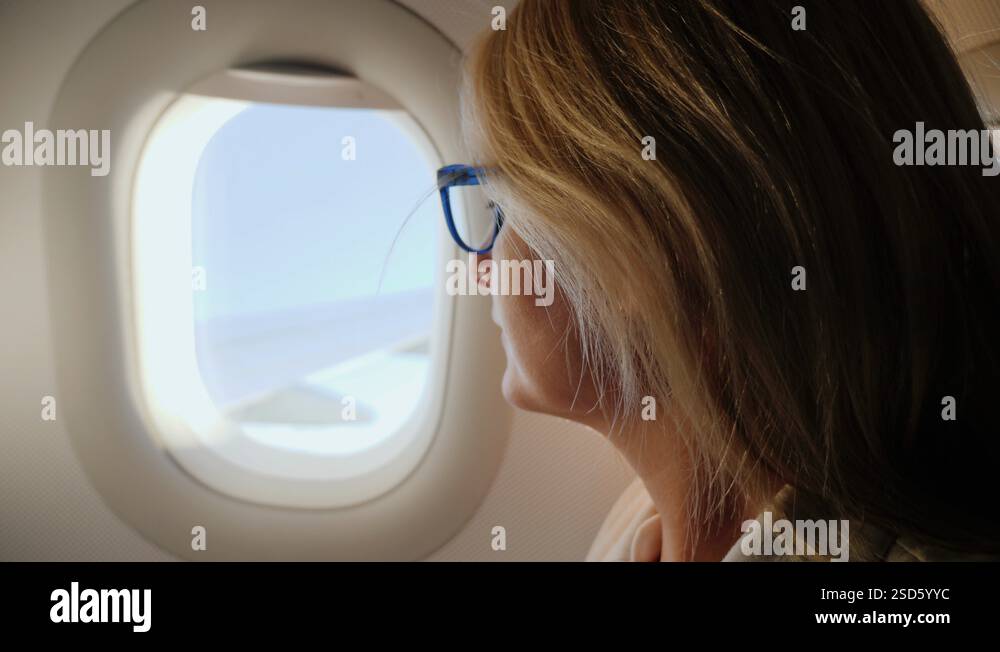 Business woman with glasses flying in an airplane, looking out the ...
