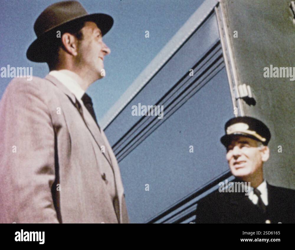 1950s: Man waves to person on train at station. Conductor looks out ...