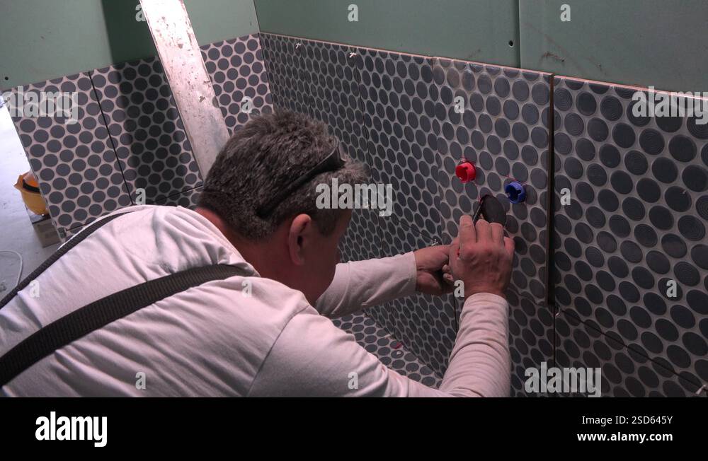 Skilled worker man make marks on tile to enlarge holes around water ...