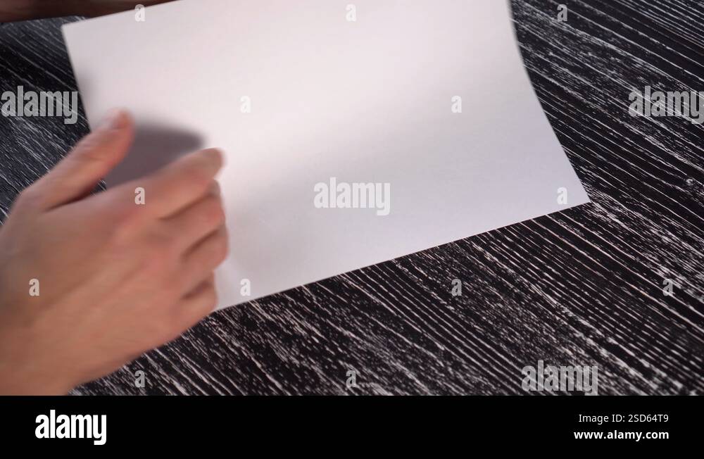 A young man makes an origami plane from a white sheet of office paper ...