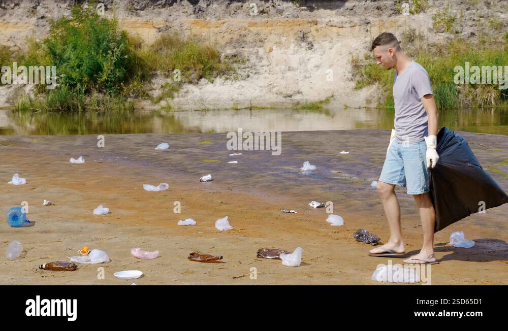 Man collects plastic trash on the banks of a dry and polluted river or ...