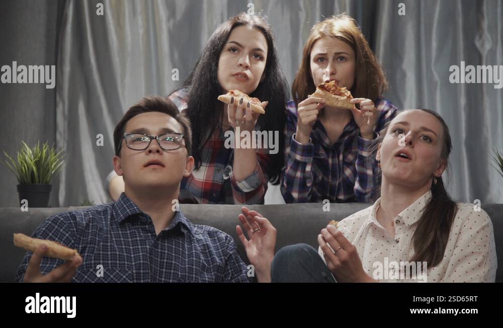 Four friends eating pizza and watching tv shows on couch in home ...