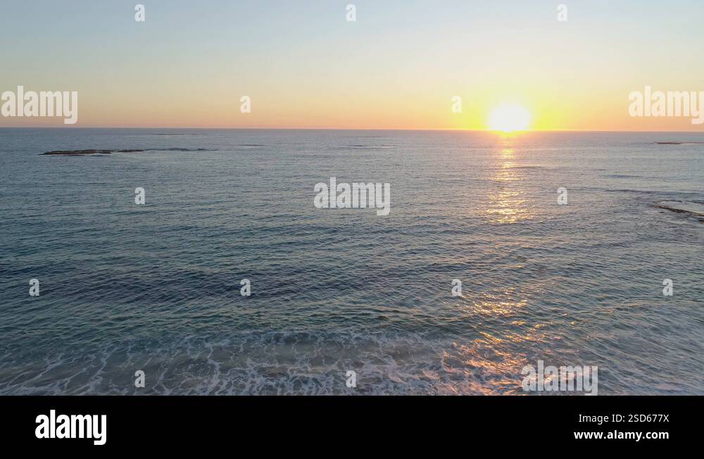 Forward flight over sea facing the sun touching the horizon at sunset ...