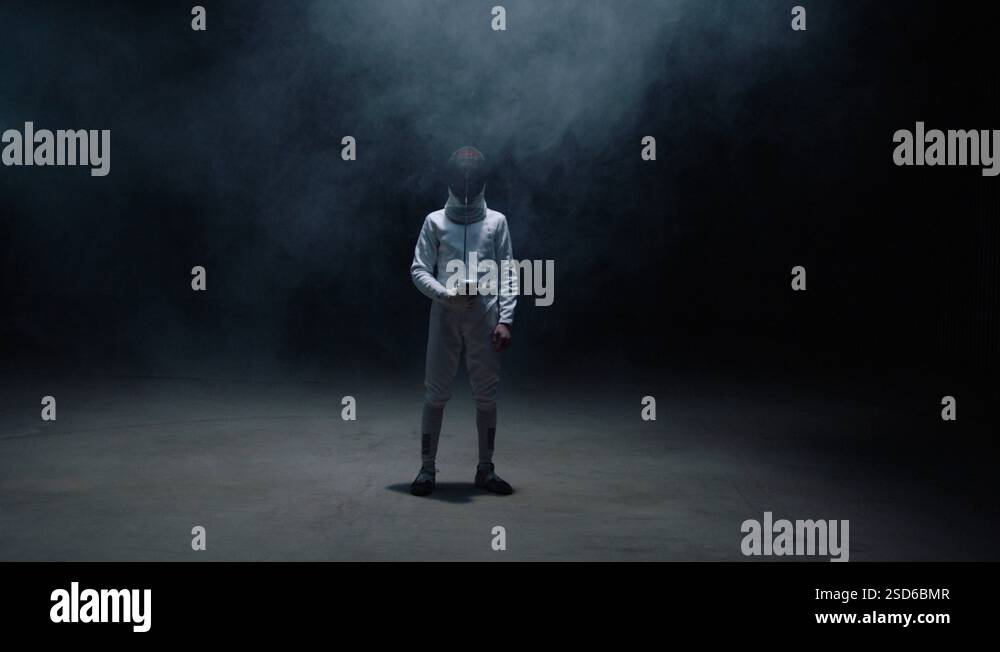 Professional fencer in uniform practicing maneuvers with sword in dark ...