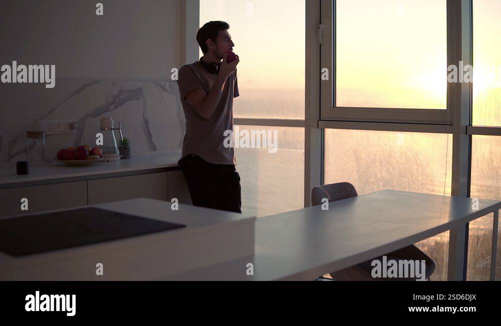 Tall, young single man with headphones on neck relaxing by the window ...