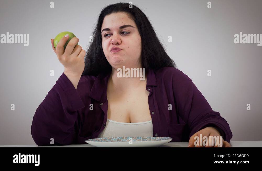 Depressed young Caucasian fat girl eating apple. Fat woman putting ...