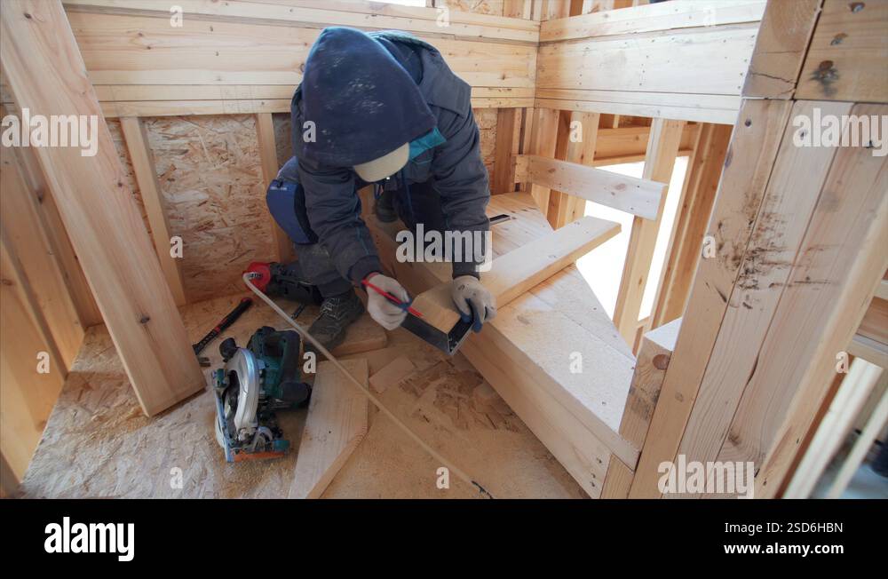 Worker measures plank to cut it with circular saw. Ladder construction ...