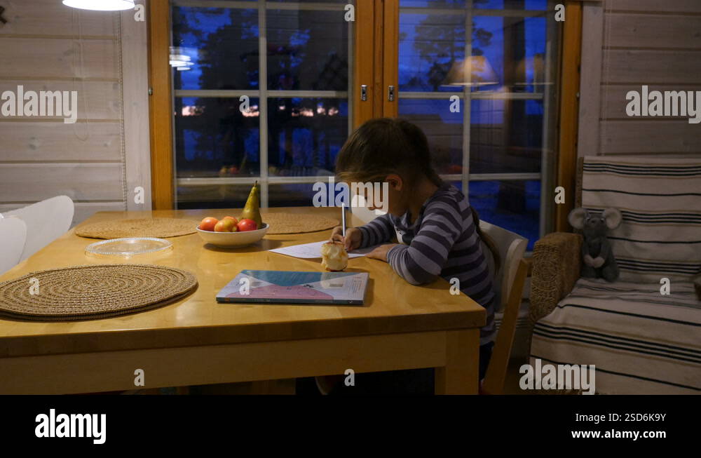 Pretty school girl at home, writing a homework. Child sitting at table ...