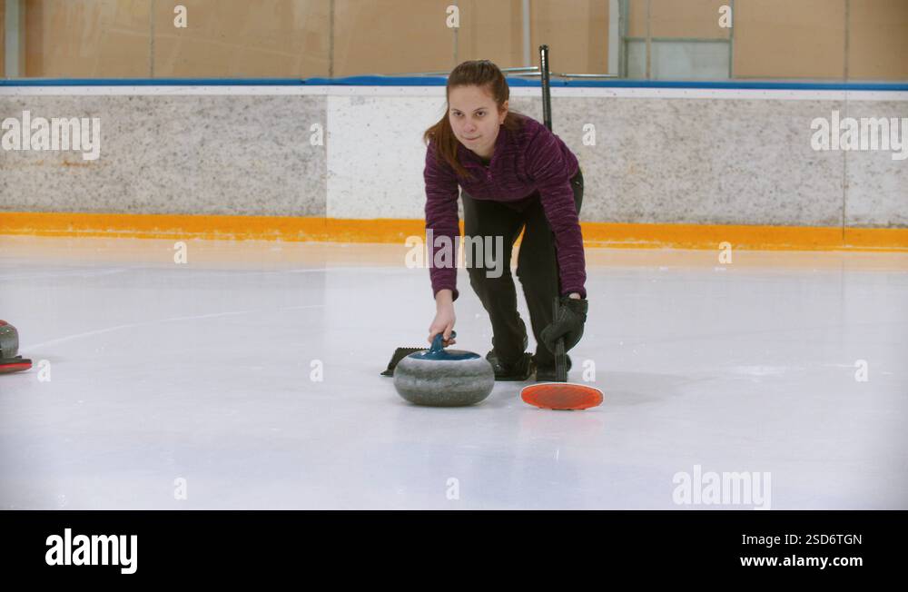 Curling training on ice rink - a young woman pushes off from the stand ...