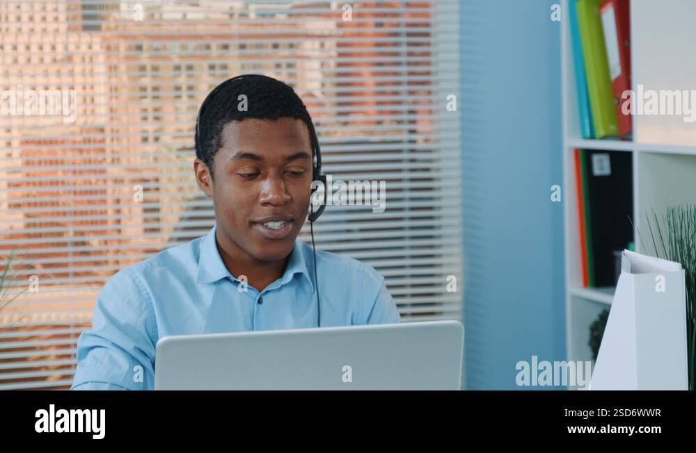 Close-up of black man in headset speaking with somebody and working on ...