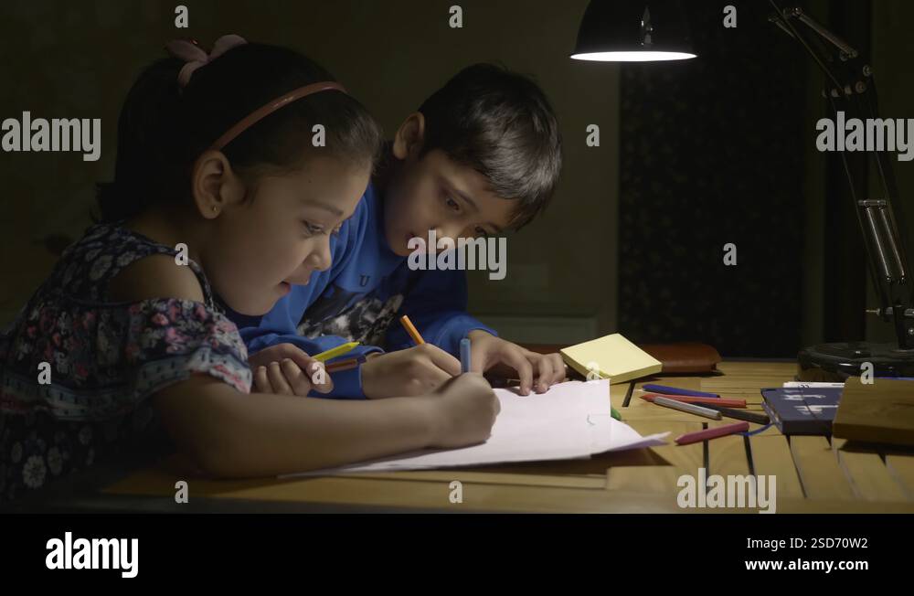 Two Indian kids drawing on a white paper under a table lamp Stock Video ...