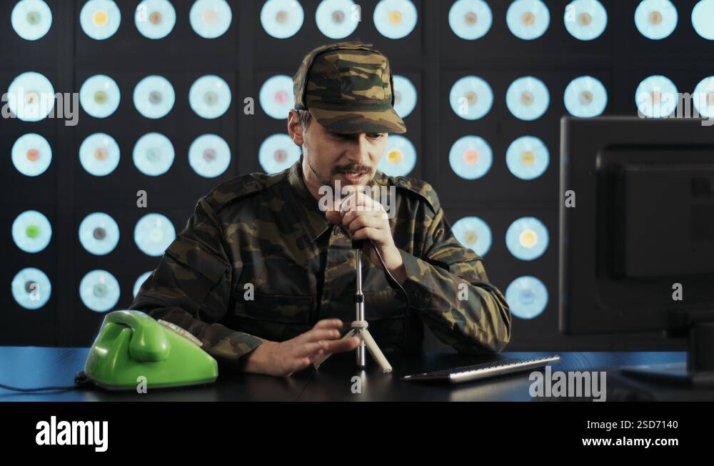 Guy in camouflage uniform at desk with PC speaks via paging microphone ...