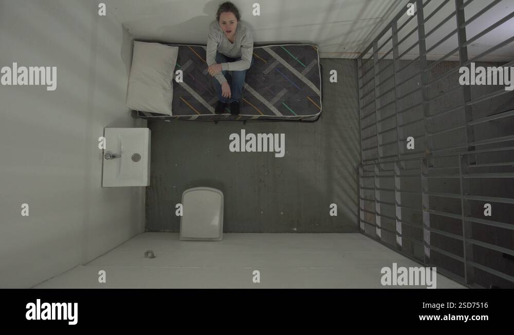 Female Prisoner in Prison Cell. The woman is sat in bed. Aerial view ...