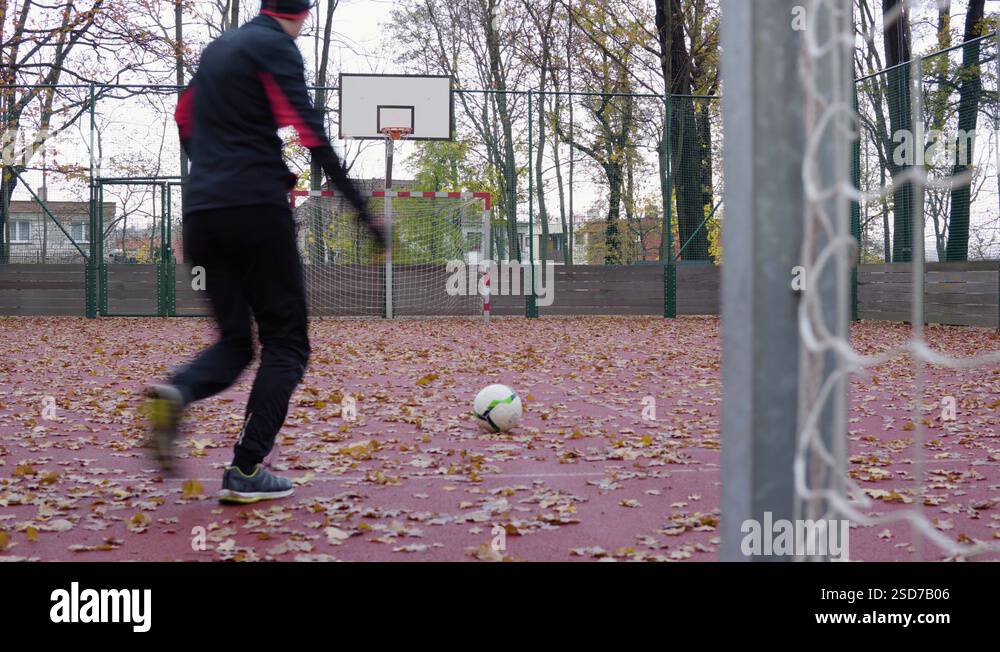 A young man kicks a soccer ball into a net in an outdoor sports field ...