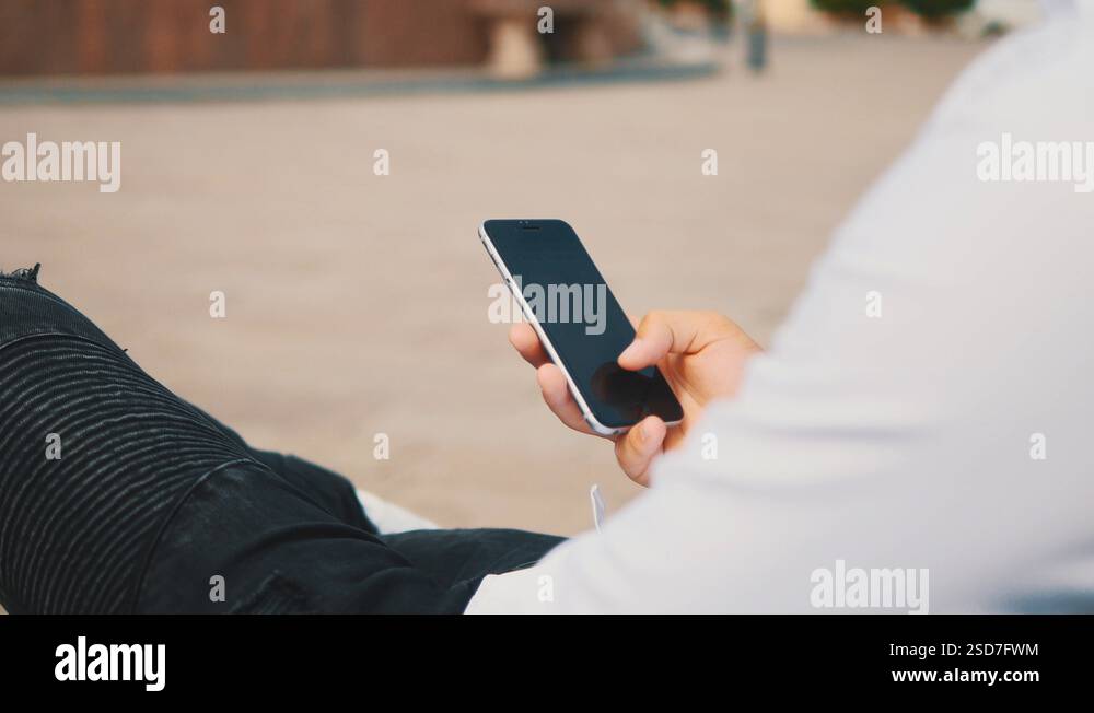 Always in touch. Young man is using smartphone outside, while sitting ...