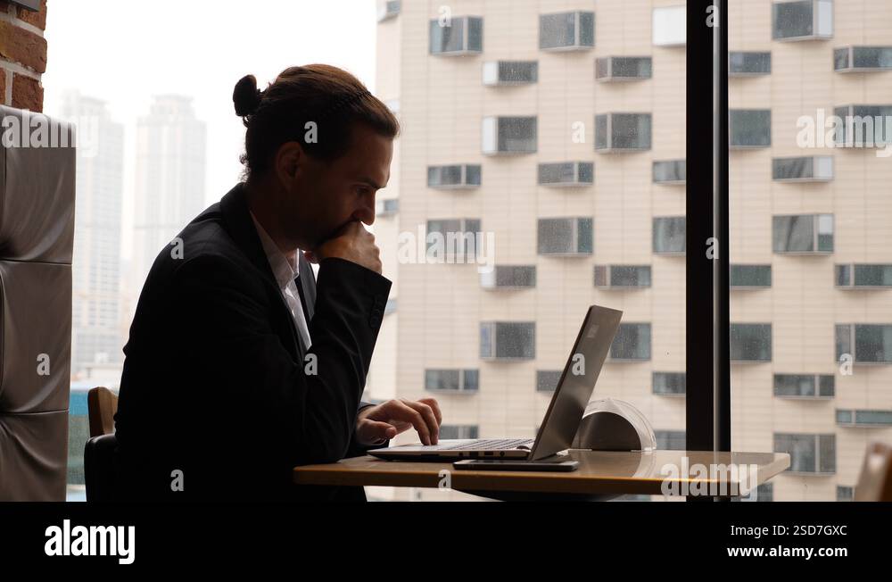 Young adult man thinking against laptop, put chin on hands, elbows on ...