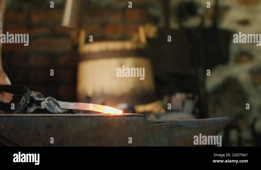 A blacksmith works in a forge, a close-up of the anvil and the red-hot ...