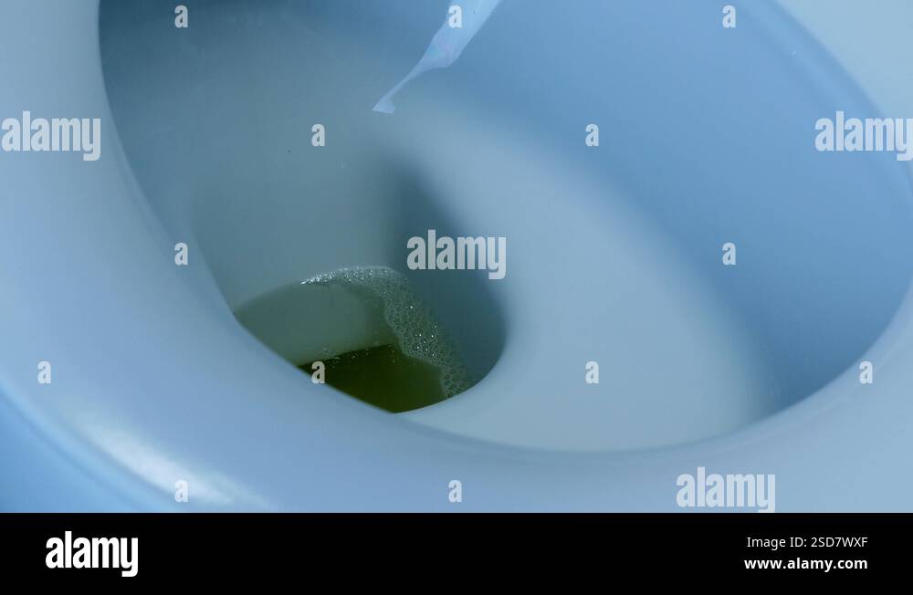 Male hand flushes urine in white toilet bowl, close up. Side view of ...