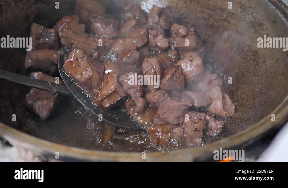 The cook throws pieces of meat into a hot iron pot. mixes the meat ...