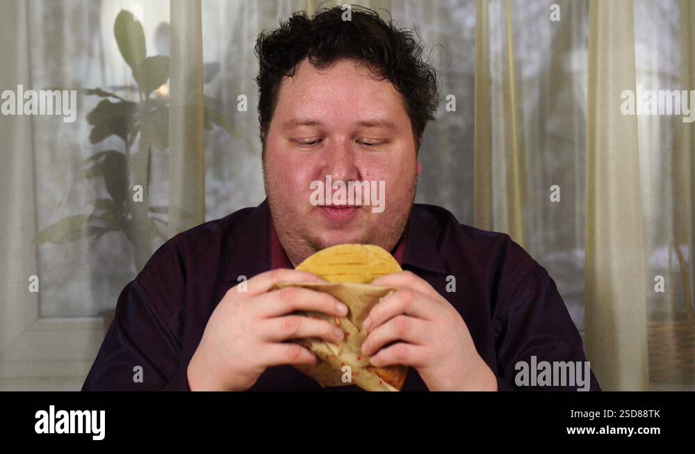 Young man bites sandwich. Fat guy eats fast food. Very hungry guy Stock ...