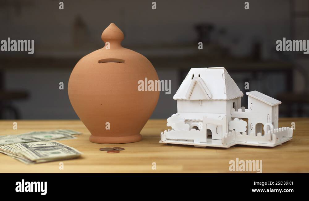 Woman putting coins into clay money near a white model of a new house ...