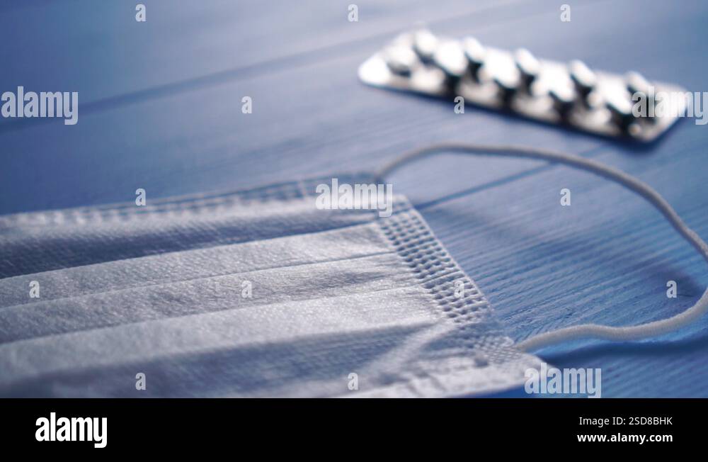 A medical mask falls next to a blister pack of green capsules on a blue ...