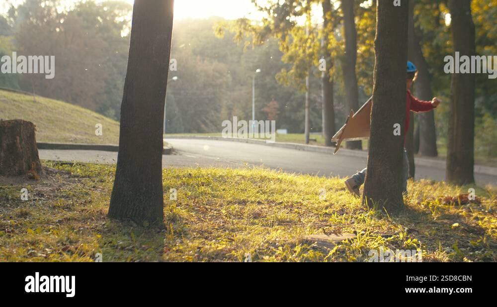 Cute small Caucasian boy in helmet and carton wings running around tree ...