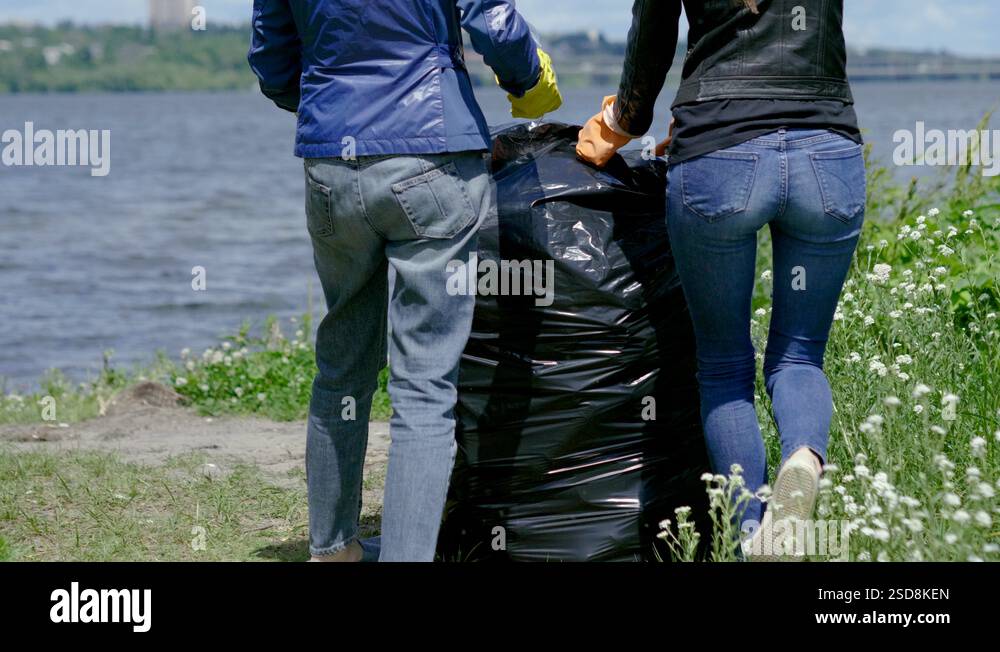Two girls picking up a garbage in bag. Young women cleaning beach from ...