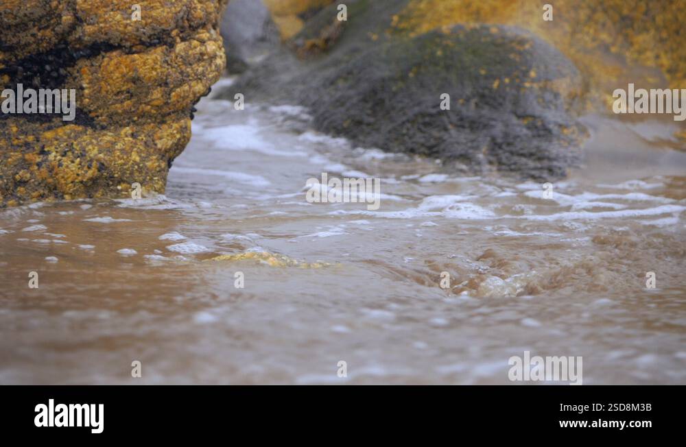 Water flowing aggressively back to ocean through beach with rocks ...