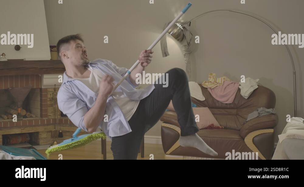 Cheerful adult Caucasian man imitating playing guitar on mop. Joyful ...