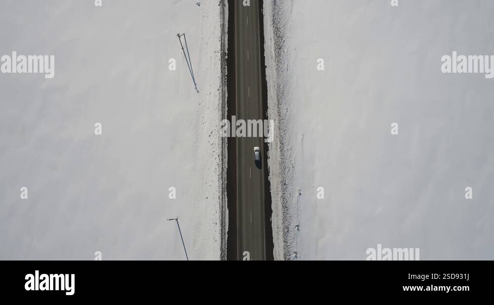 One car driving into the distance on straight road throught snow field ...