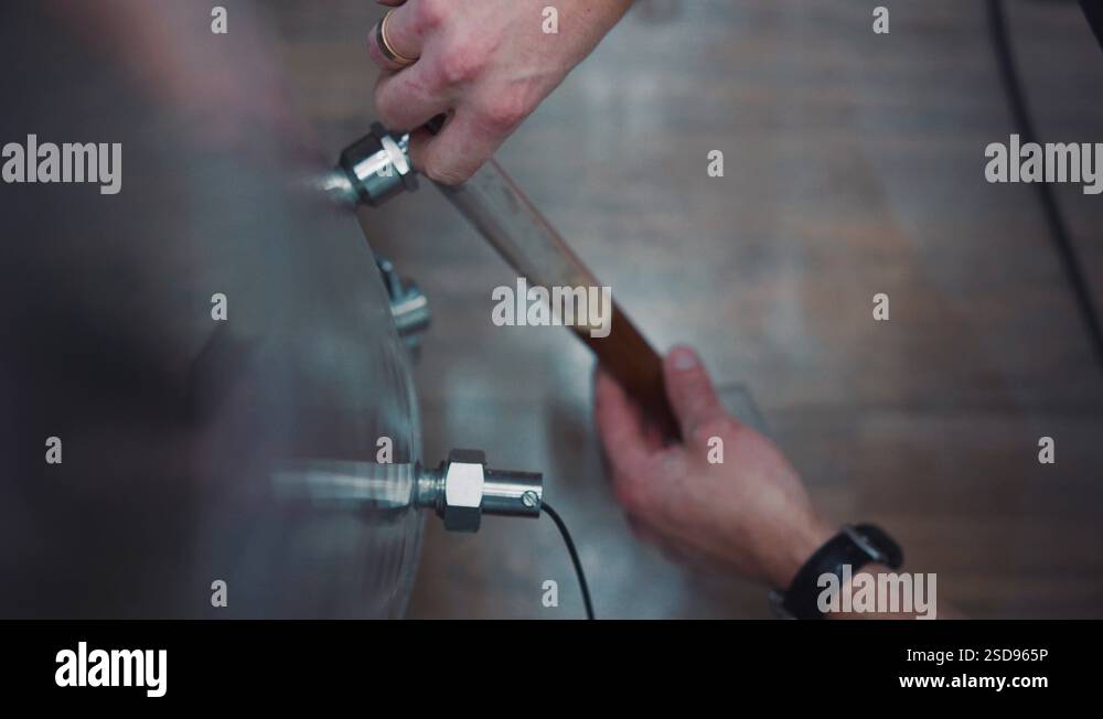 Men pouring beer liquid in a little tube from a big boiler with a tap ...