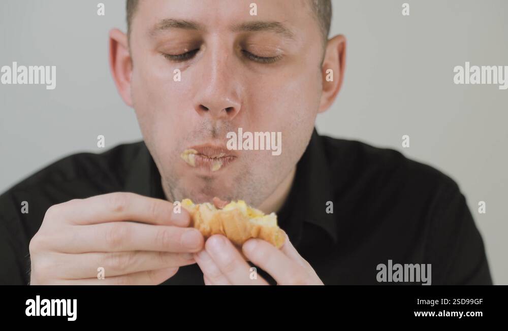 Man eating croissant with egg and sausage. Emotionally chewing on the ...