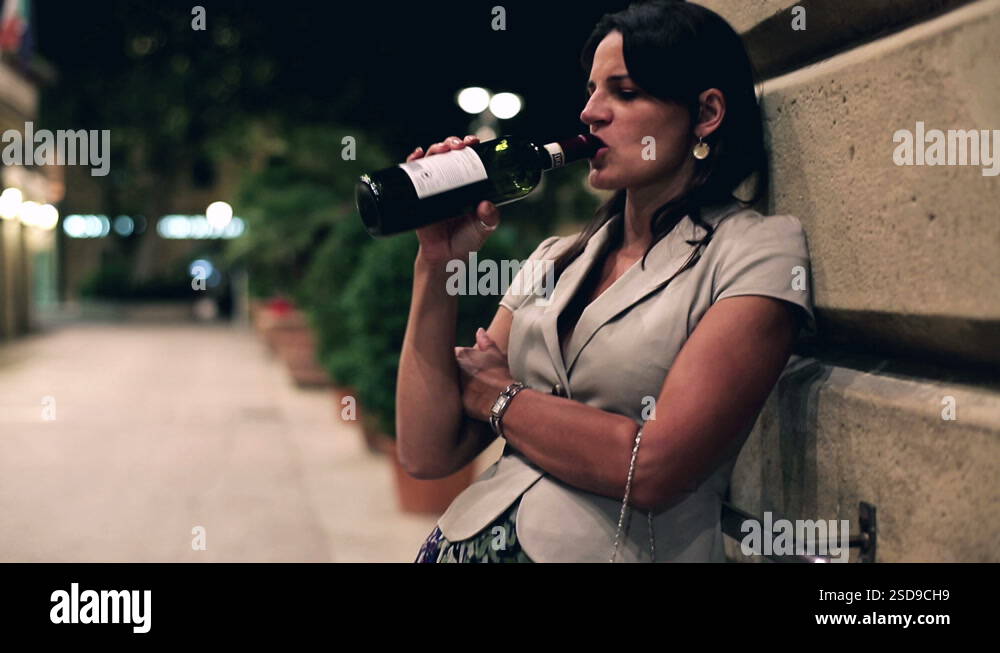 Drunk couple with bottle of wine standing on street in the evening ...