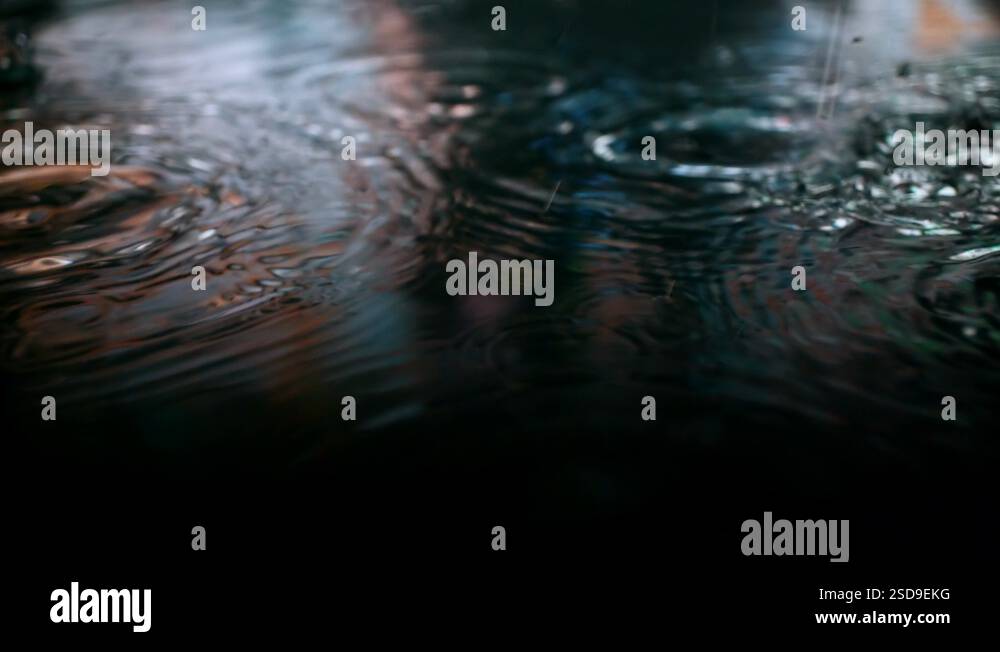 Rain drops falling into puddle at night. City street reflection on ...