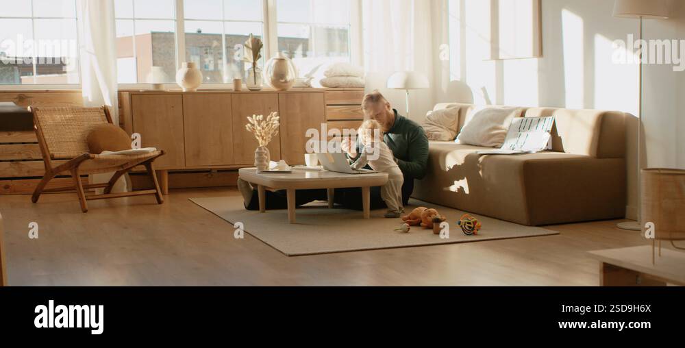 Father working from home alone, feeding his daughter in front of laptop ...