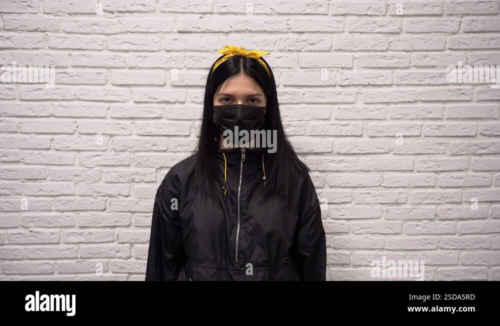 Woman in mask looks frown and seriously on a white brick wall background Stock Video Footage - Alamy