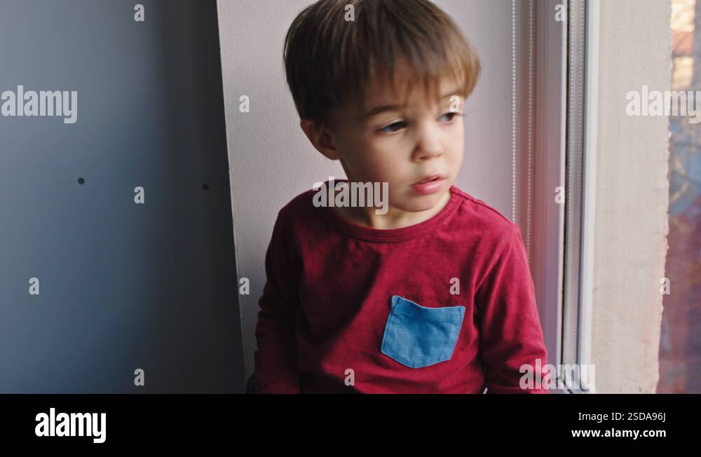 Charismatic small cute boy looking sad through the window he stay at ...