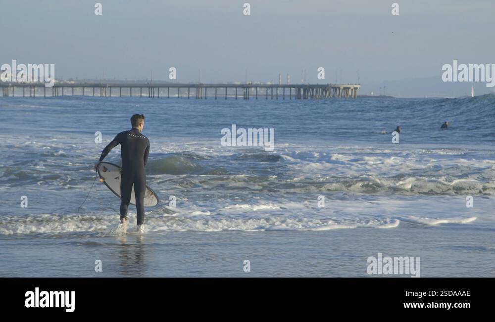 A surfer washing his board in the ocean before heading out to surf at ...