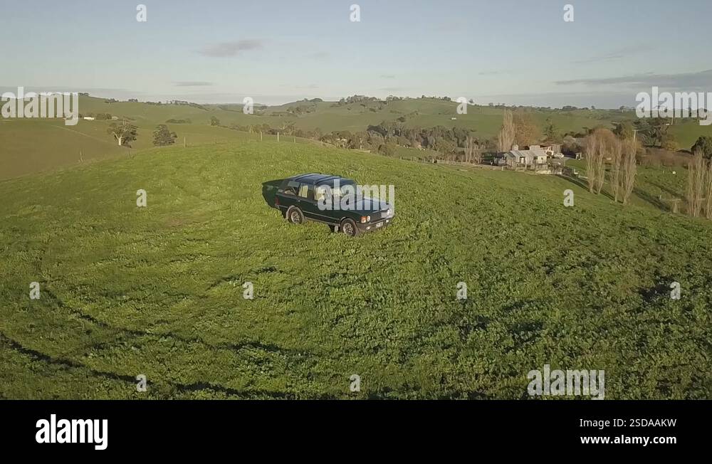 Slow pull away aerial shot of classic 4wd SUV on top of grassy hill ...