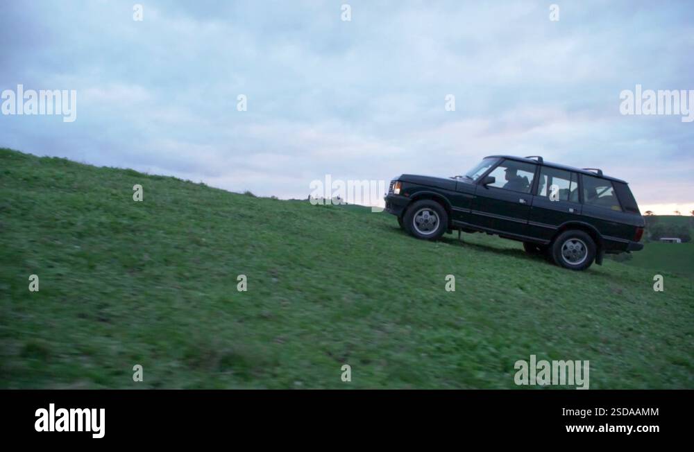 Slow motion tracking shot of classic 4WD SUV driving up a grassy hill ...