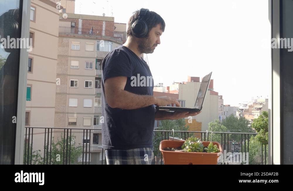 Man in pajamas with laptop working on the balcony of his house in Spain ...