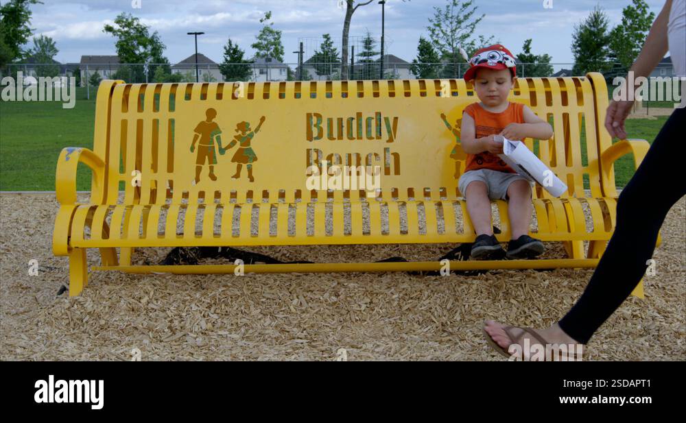 Teacher sits down next to toddler boy sitting on buddy bench alone ...